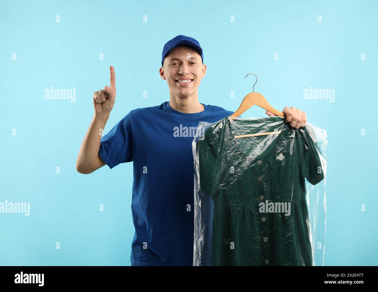 Dry-cleaning delivery. Happy courier holding dress in plastic bag and ...