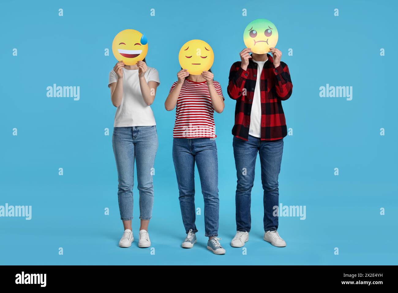 People covering faces with emoticons on light blue background Stock ...