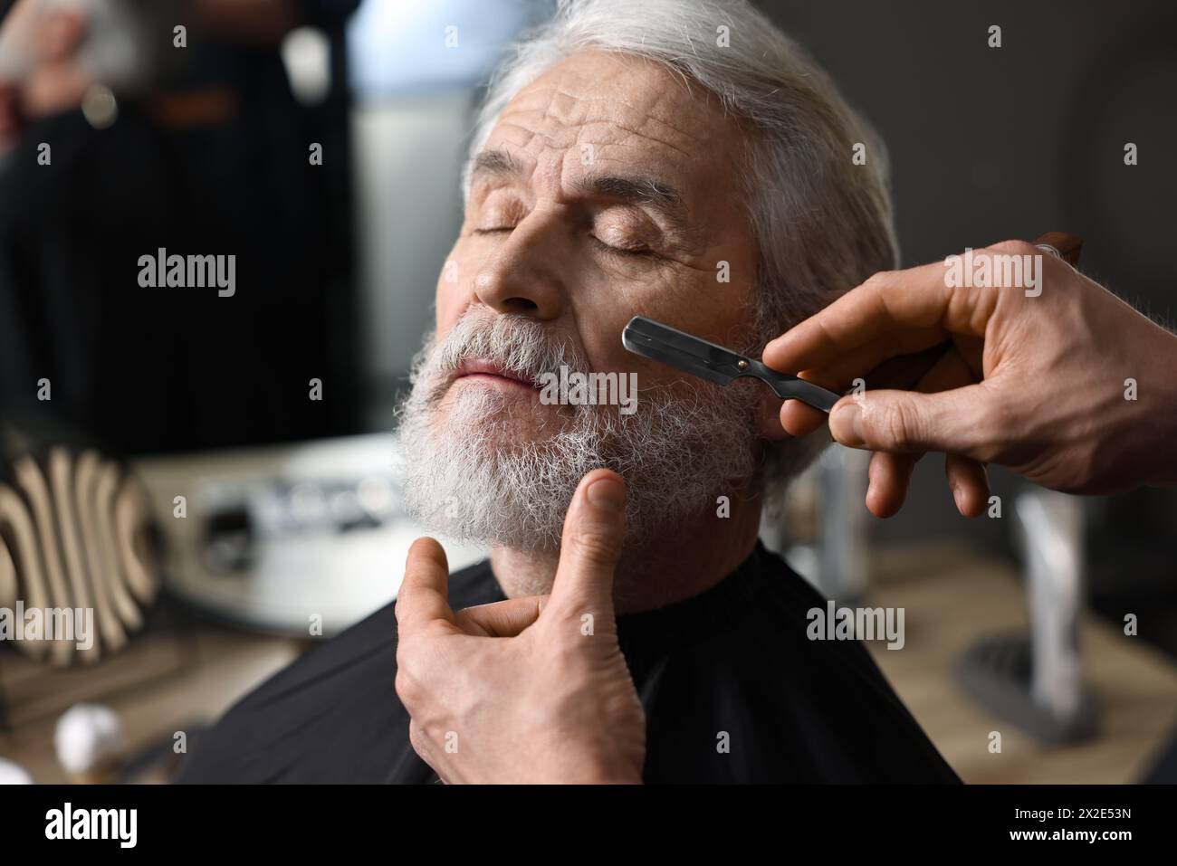 Professional barber shaving client's beard with blade in barbershop ...
