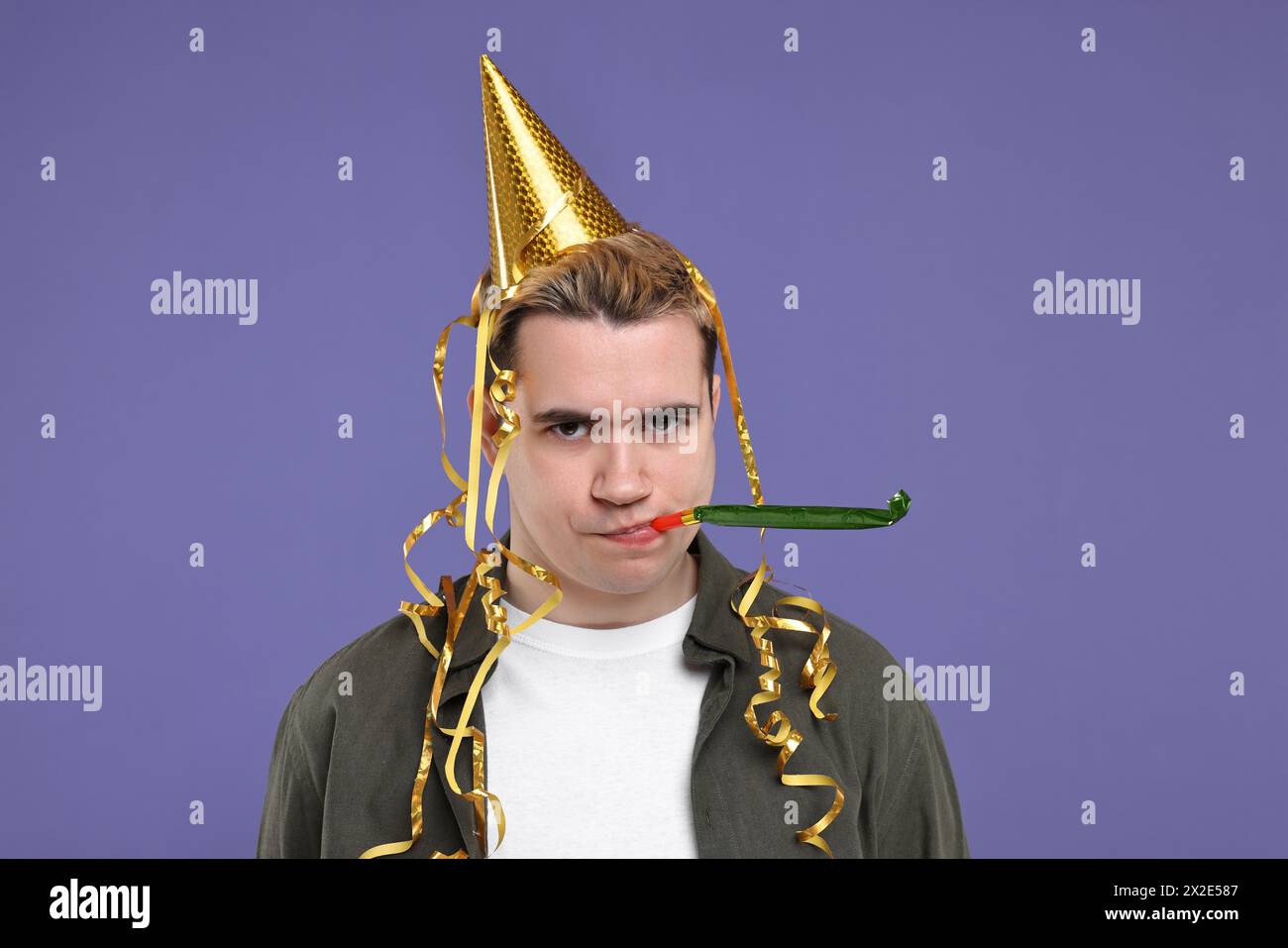 Sad young man with party hat and blower on purple background Stock ...