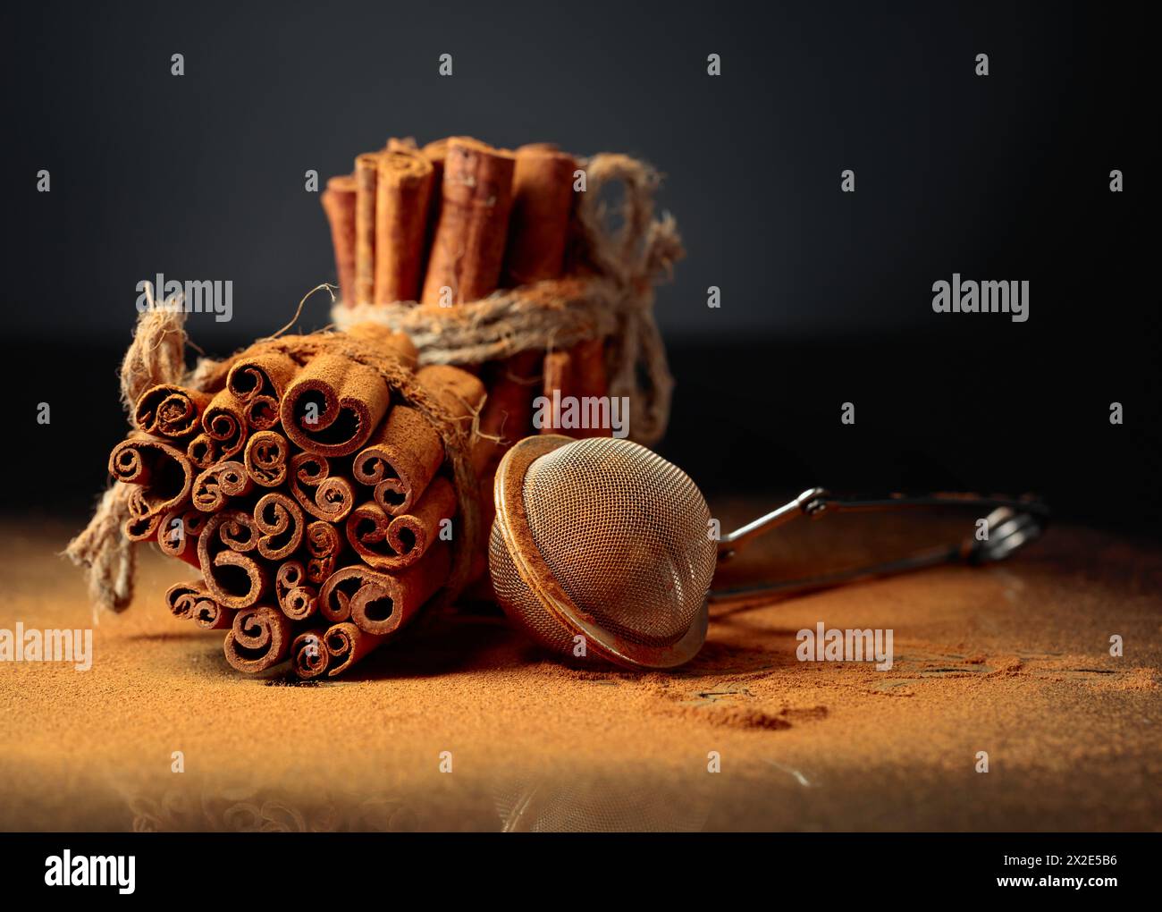 Ground cinnamon, cinnamon sticks, tied with jute rope on a black ...