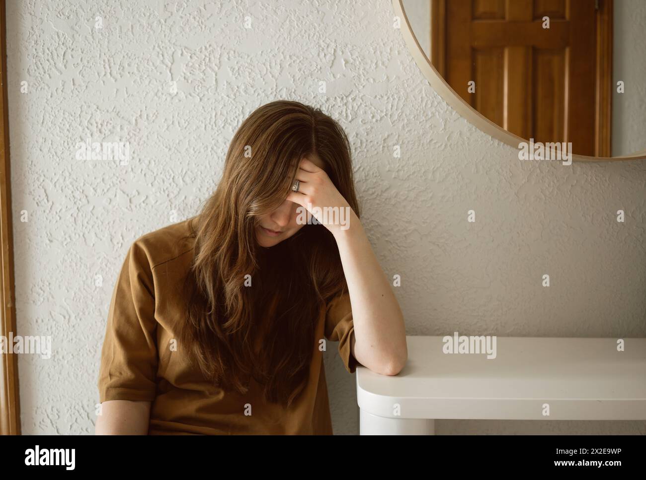 Overwhelmed woman puts head in hand and leans on table Stock Photo - Alamy