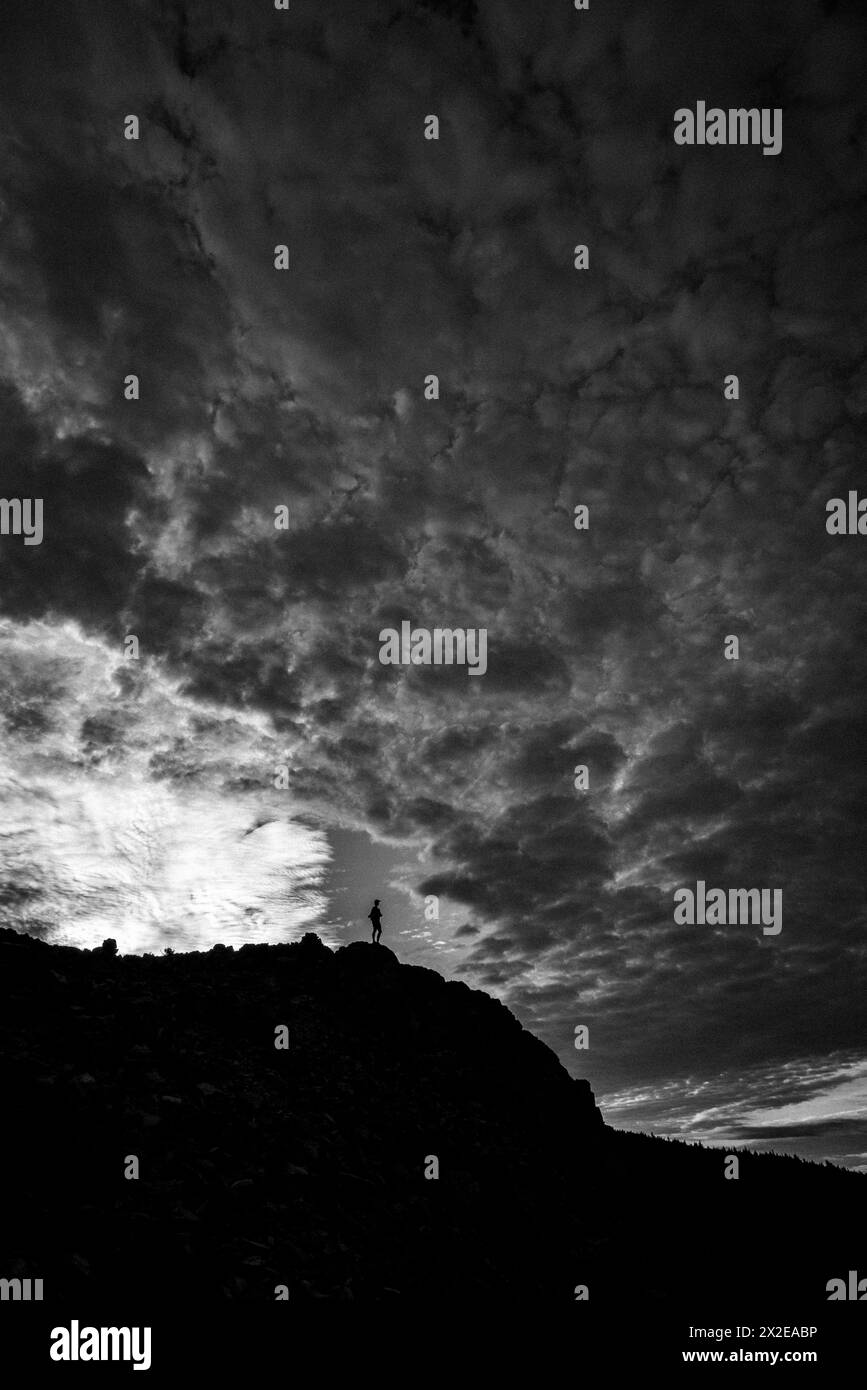 lone person perfectly aligned with break in the clouds on mountain ...