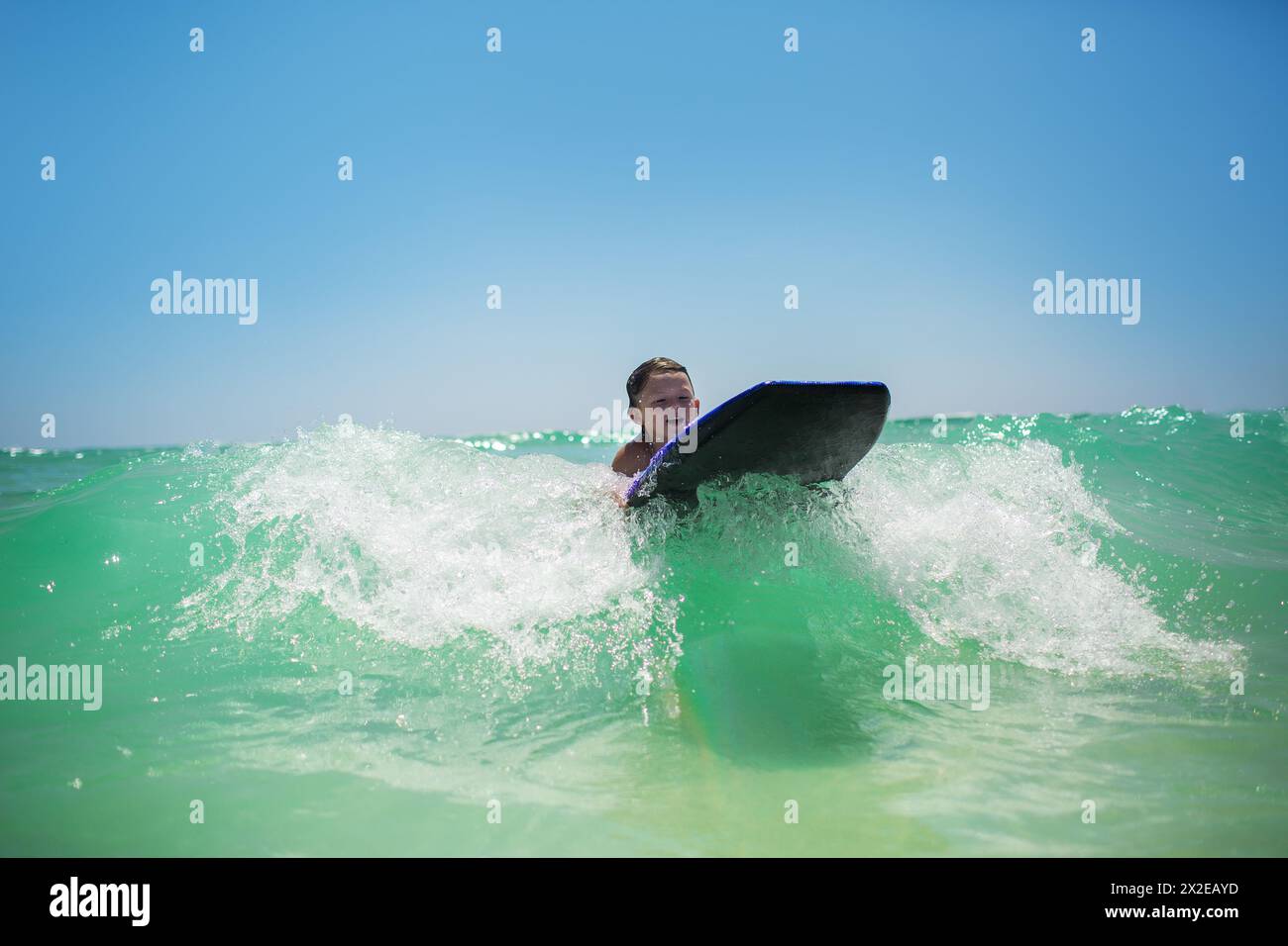 Boy on a boogie board catching waves in clear sea Stock Photo - Alamy