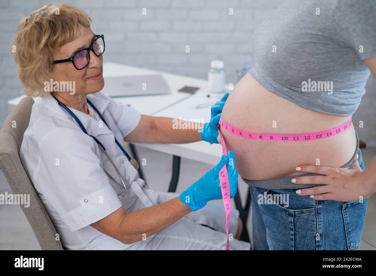 Doctor measuring the volume of a pregnant woman's abdomen using a tape ...