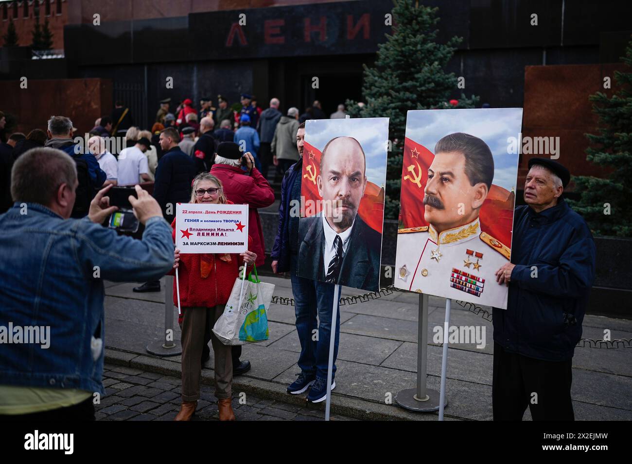 A man takes a photo of people standing with portraits of Soviet founder ...