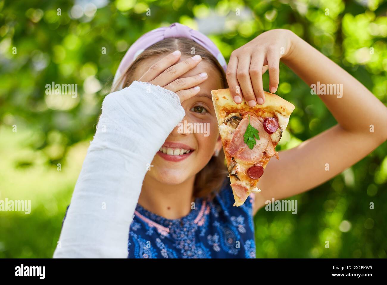 A cheerful girl with a white cast on her arm is playfully covering one ...