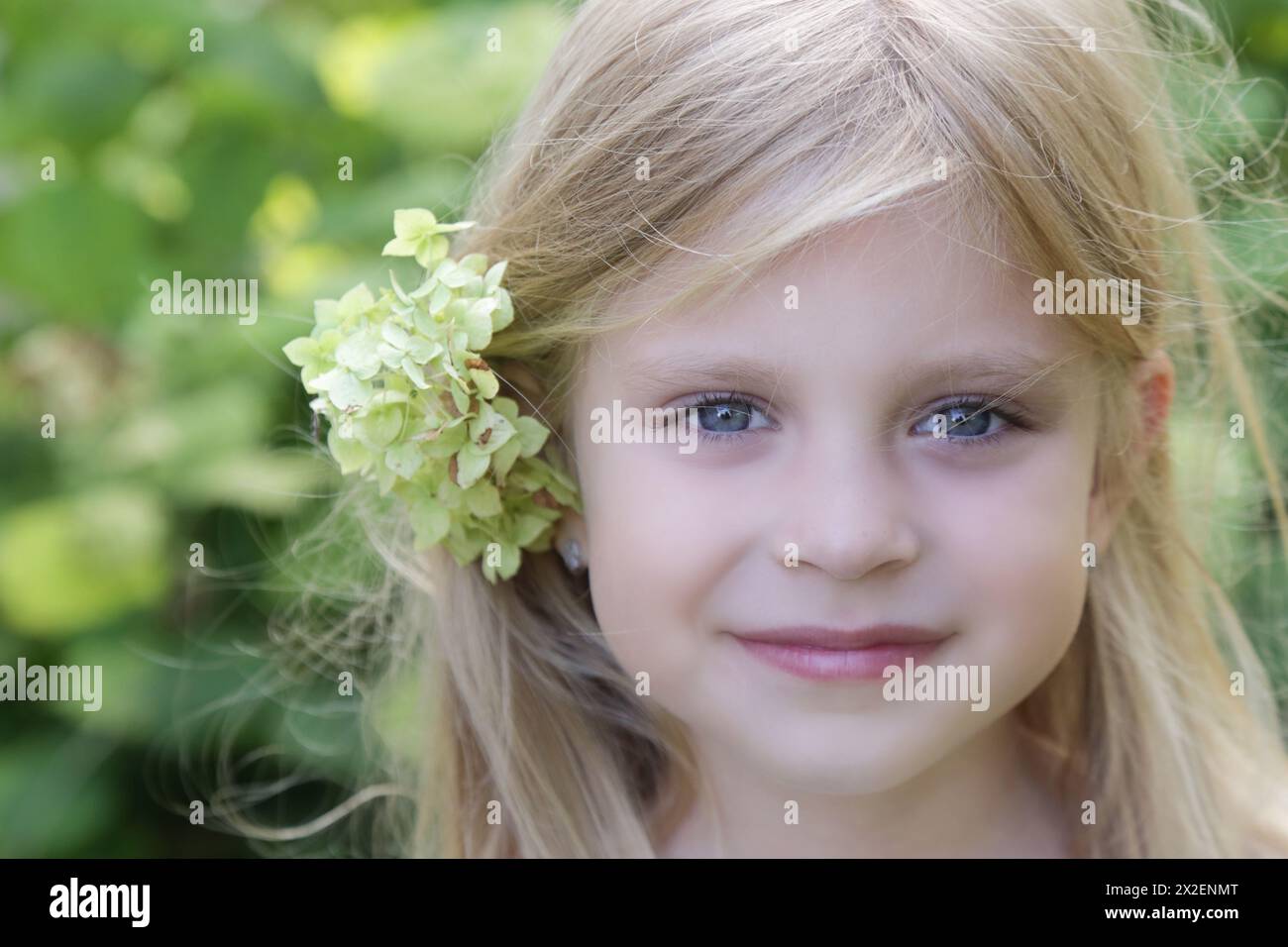 Candid outdoor portrait of happy little girl with green flower behind ...