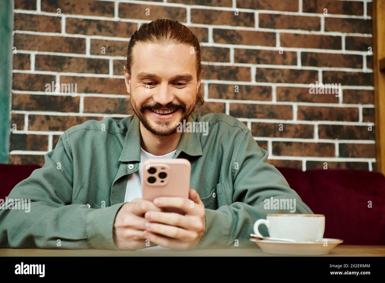 happy man is seated at a table in a modern cafe, focused on using his ...