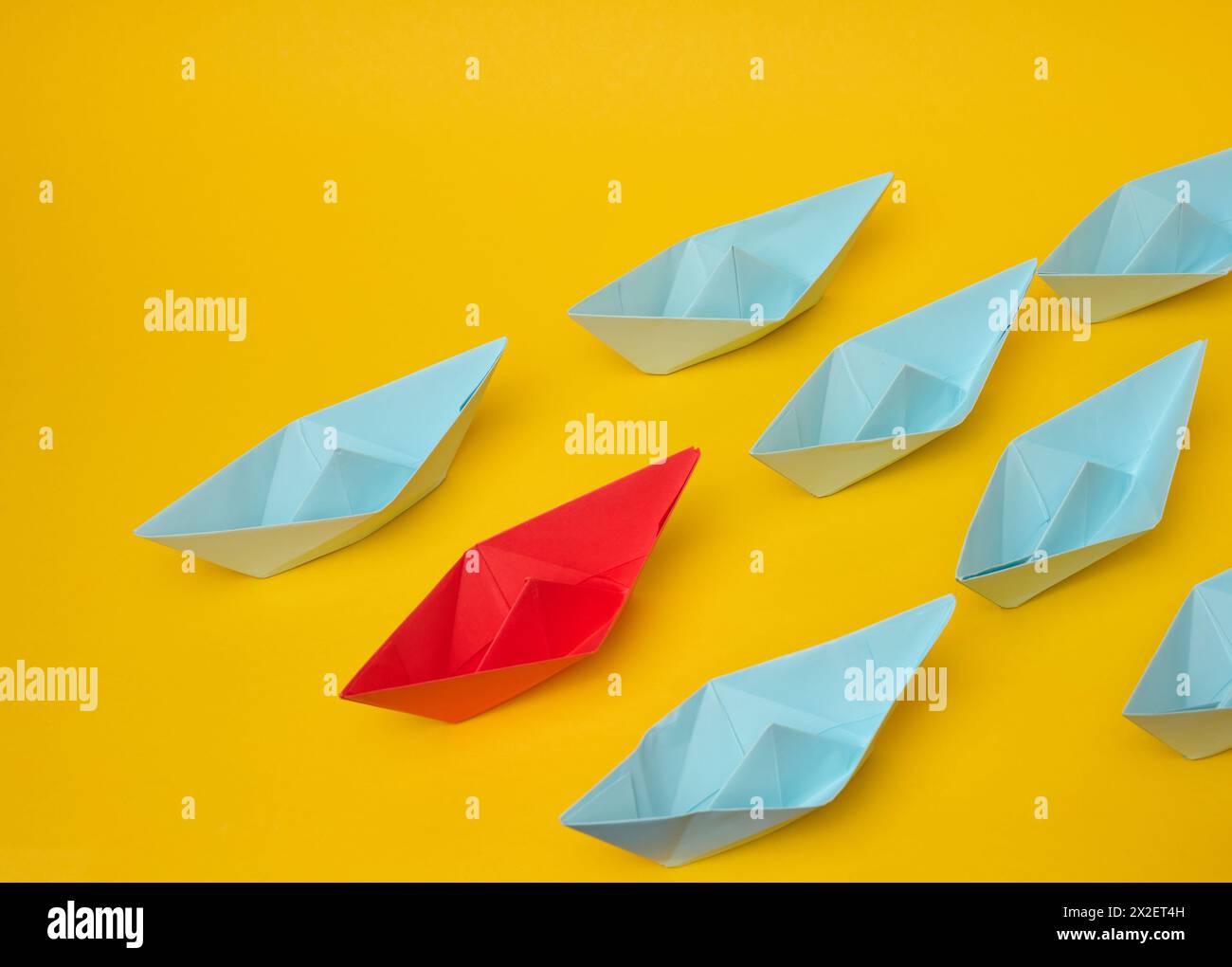 Group of blue paper boats follow red against a yellow background ...