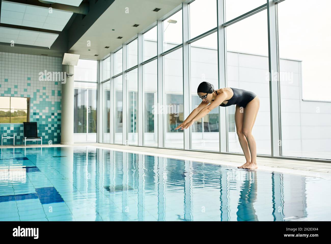 A young woman in a black bathing suit and swim cap elegantly dives into ...