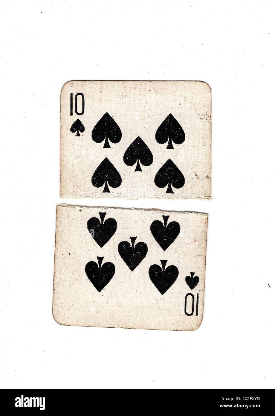 A vintage, well used ten of spades playing card torn in half on a white ...