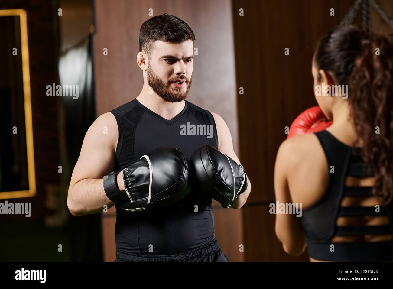 A male trainer and a brunette sportswoman boxing in a gym, showcasing ...