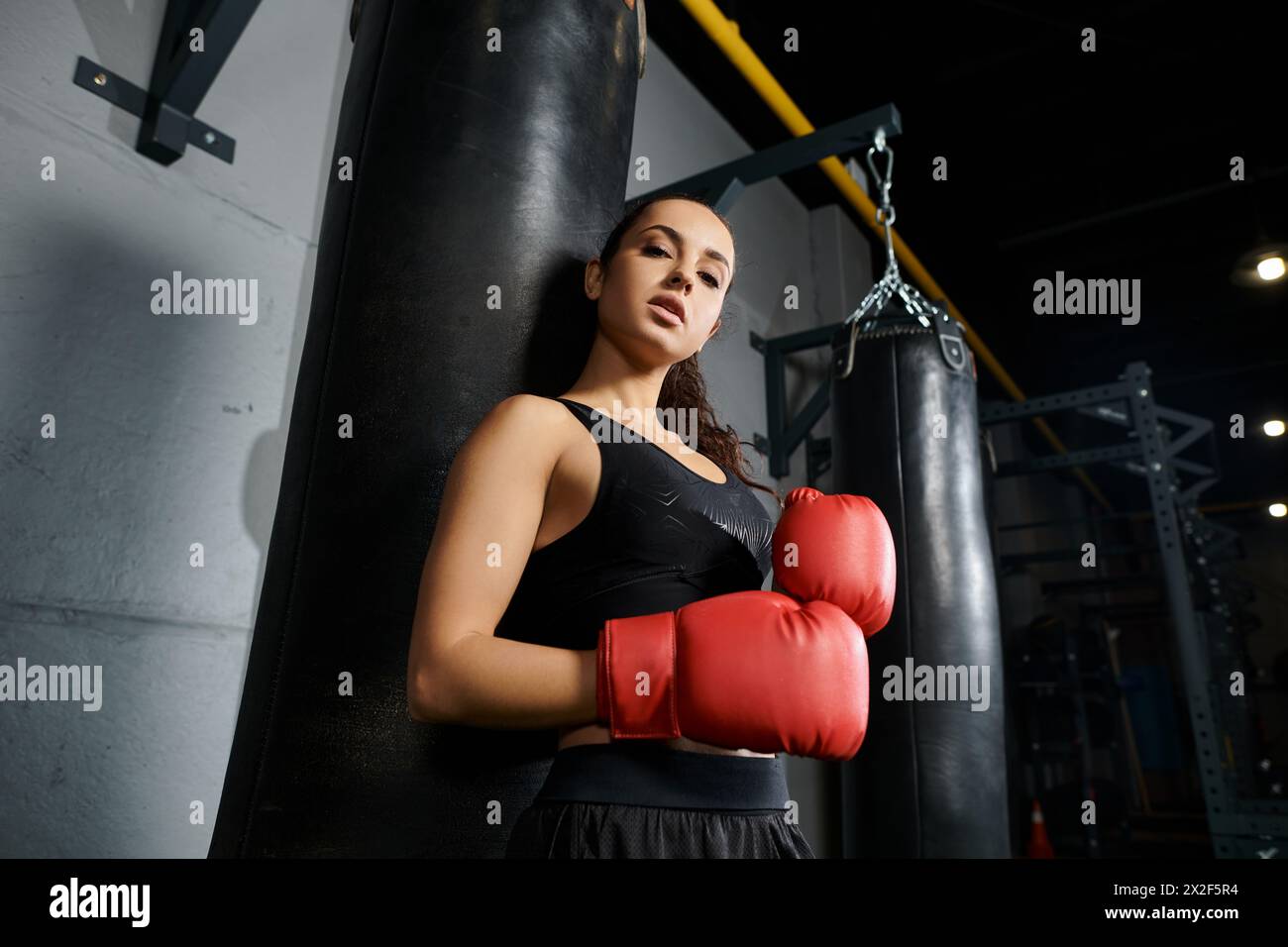 A brunette sportswoman in active wear stands next to a punching bag in ...