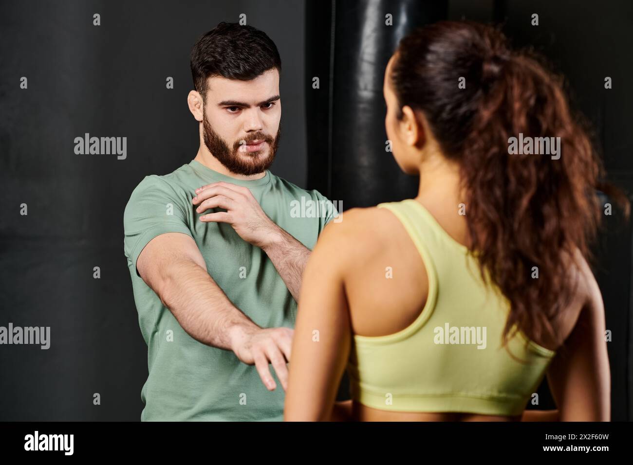 A male trainer demonstrates self-defense techniques to a woman in a gym ...