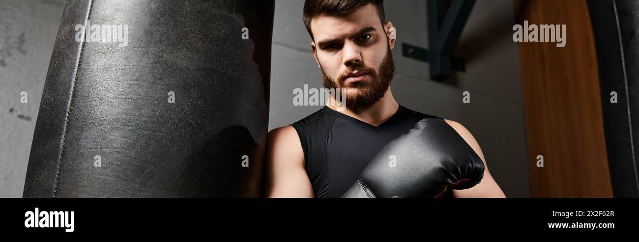 A handsome bearded man wearing boxing gloves stands next to a punching ...