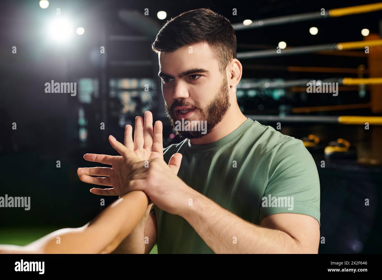 A man demonstrates self-defense techniques to a woman in a gym setting ...