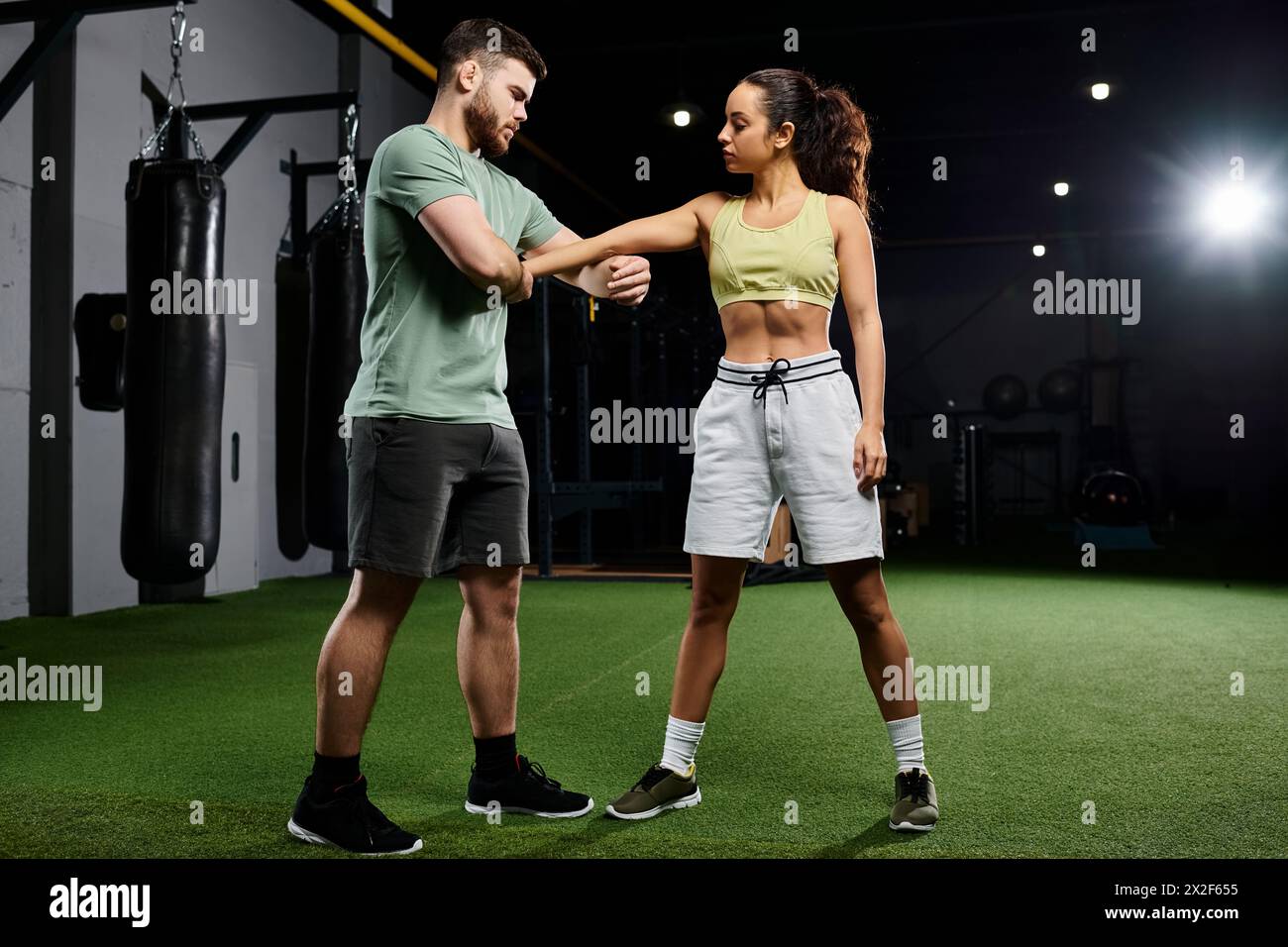 A male trainer demonstrates self-defense techniques to a woman in a gym ...