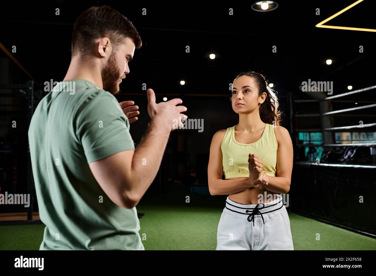 A male trainer demonstrates self-defense techniques to a woman in a gym ...