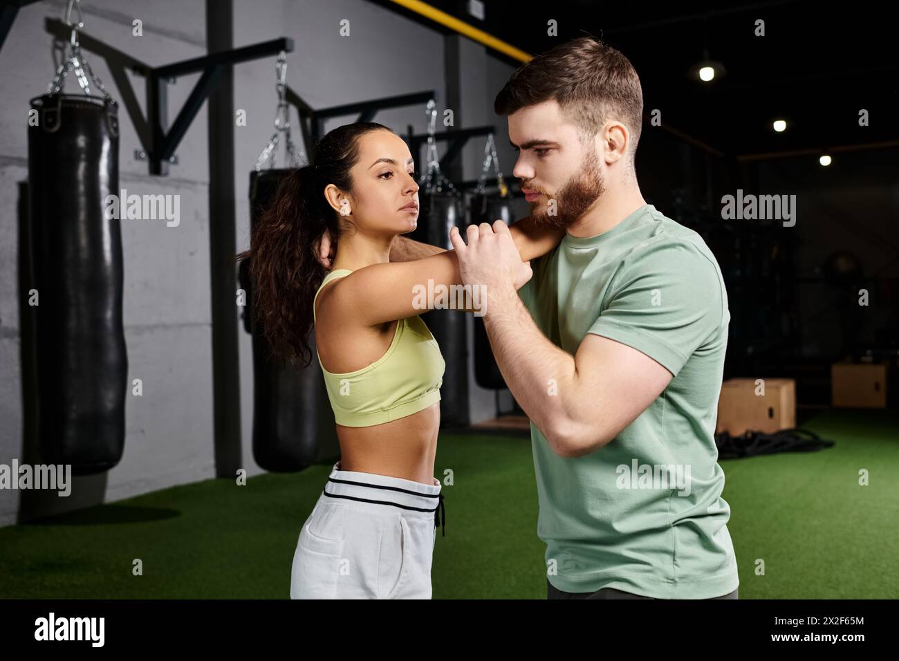 A male trainer guiding a woman through self-defense techniques in a gym ...