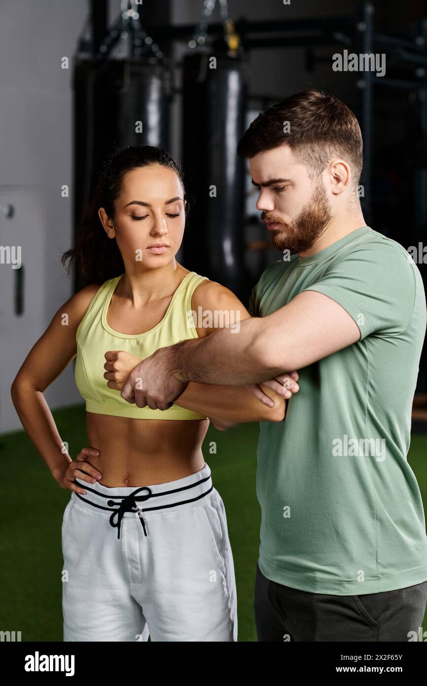 A male trainer demonstrates self-defense techniques to a woman in a gym ...