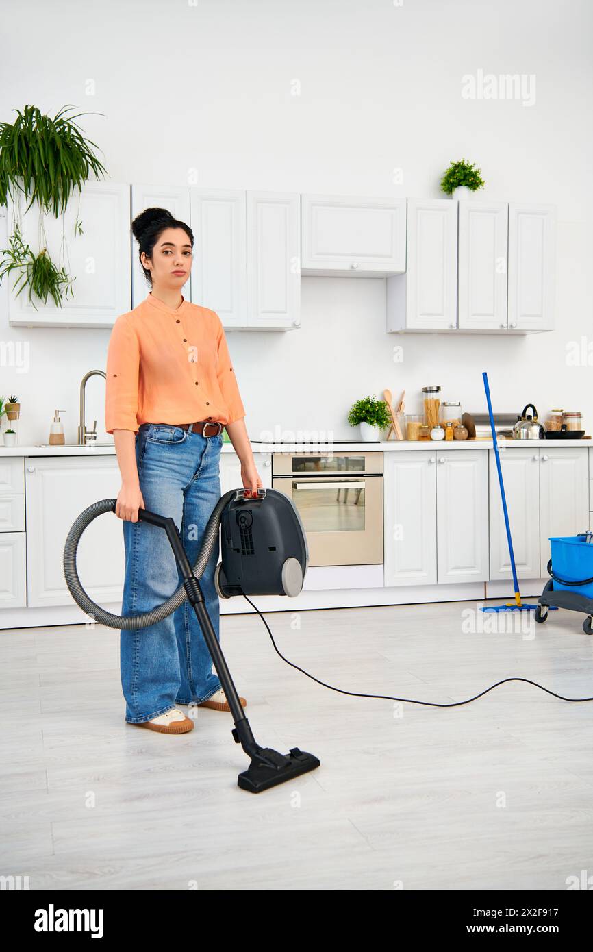 A stylish woman in casual attire gracefully vacuums the kitchen floor ...