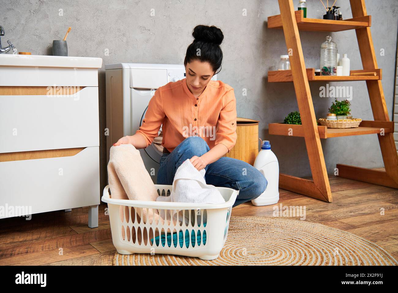 A stylish woman sits on the floor with a laundry basket in front of her ...