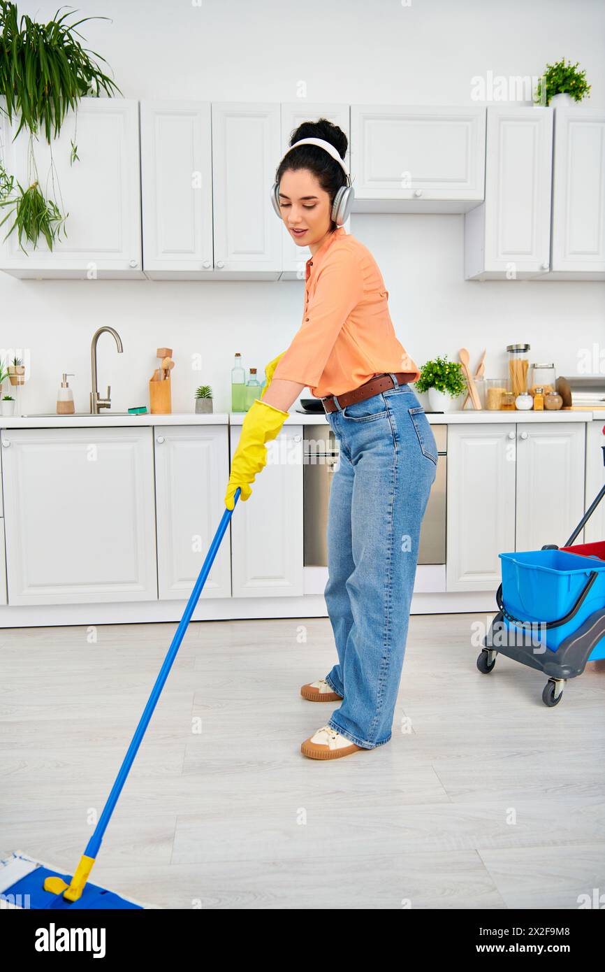 A stylish woman in casual clothing gracefully mops the kitchen floor ...