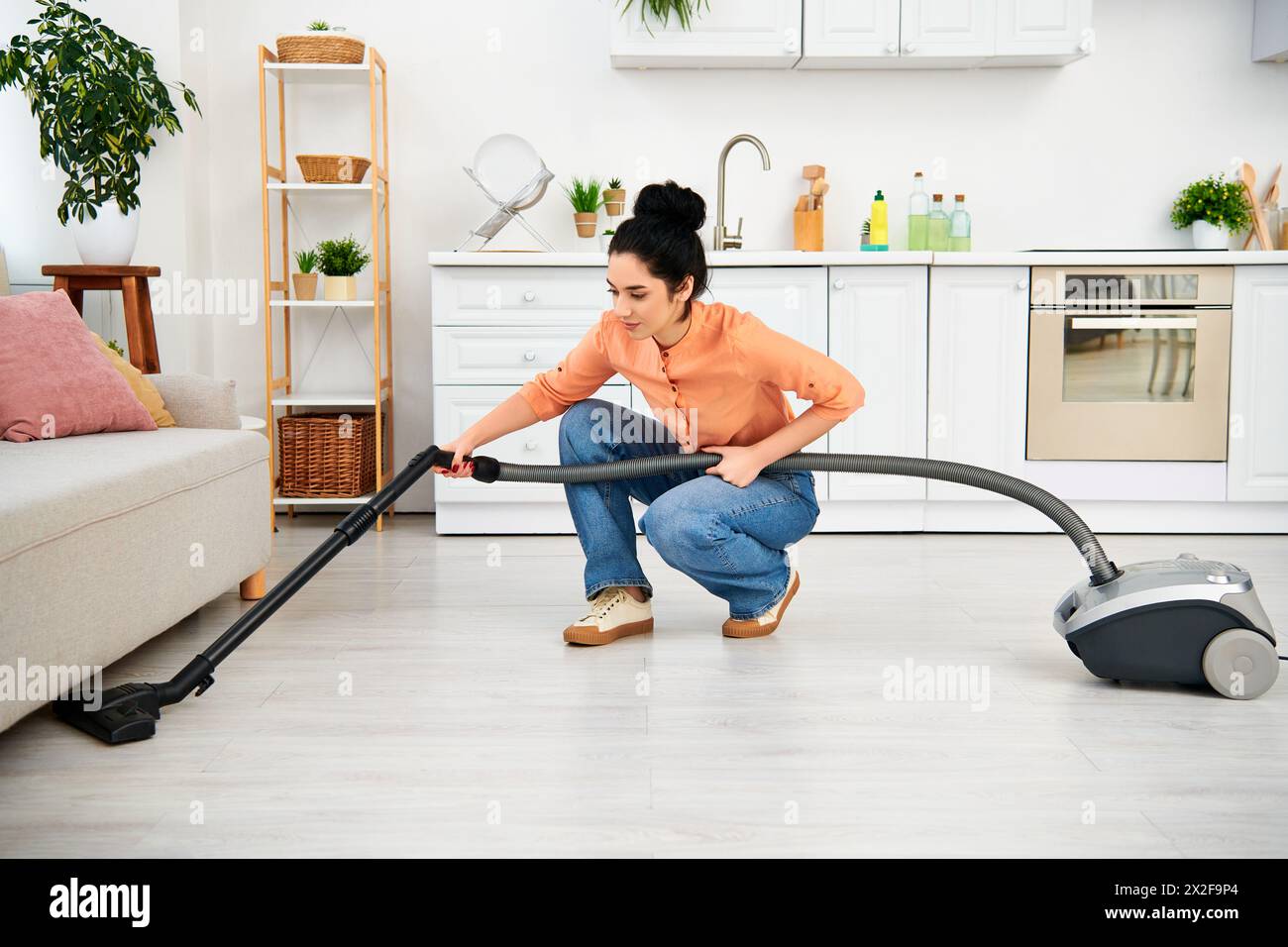 A stylish woman in casual attire gracefully vacuums the floor with her ...