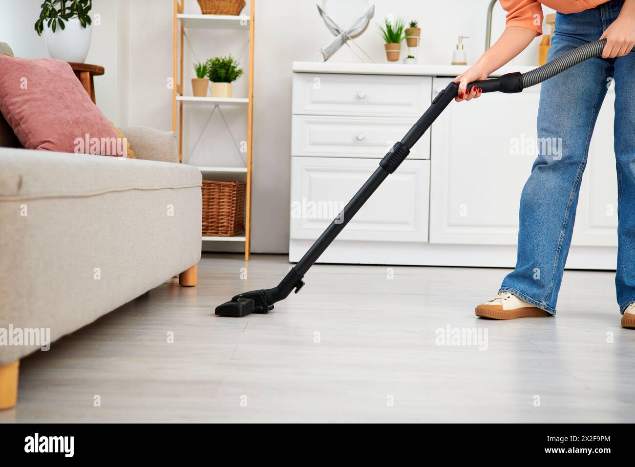 A stylish woman in casual attire using a vacuum cleaner to tidy the ...
