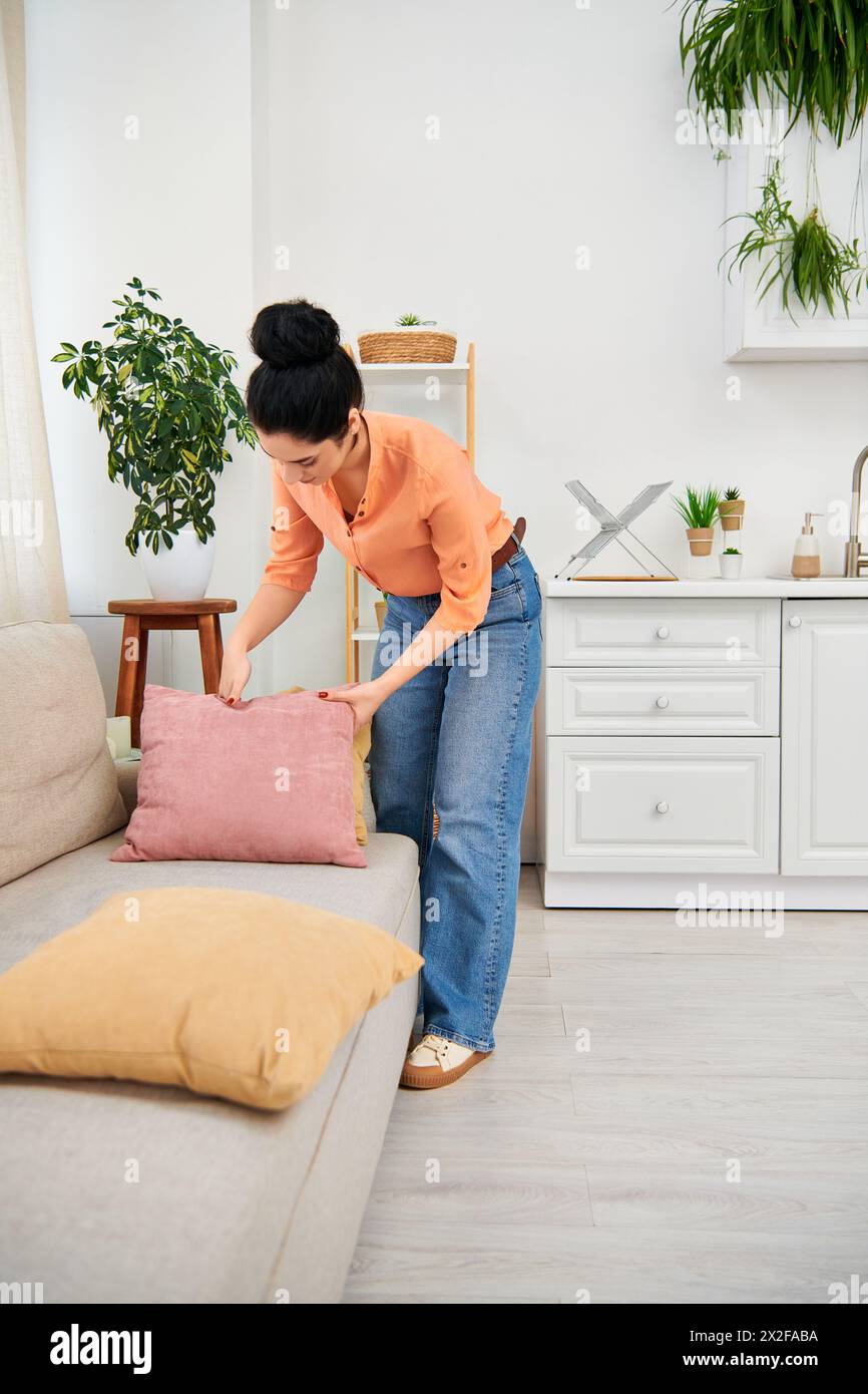 A stylish woman in casual attire carefully places a decorative pillow ...