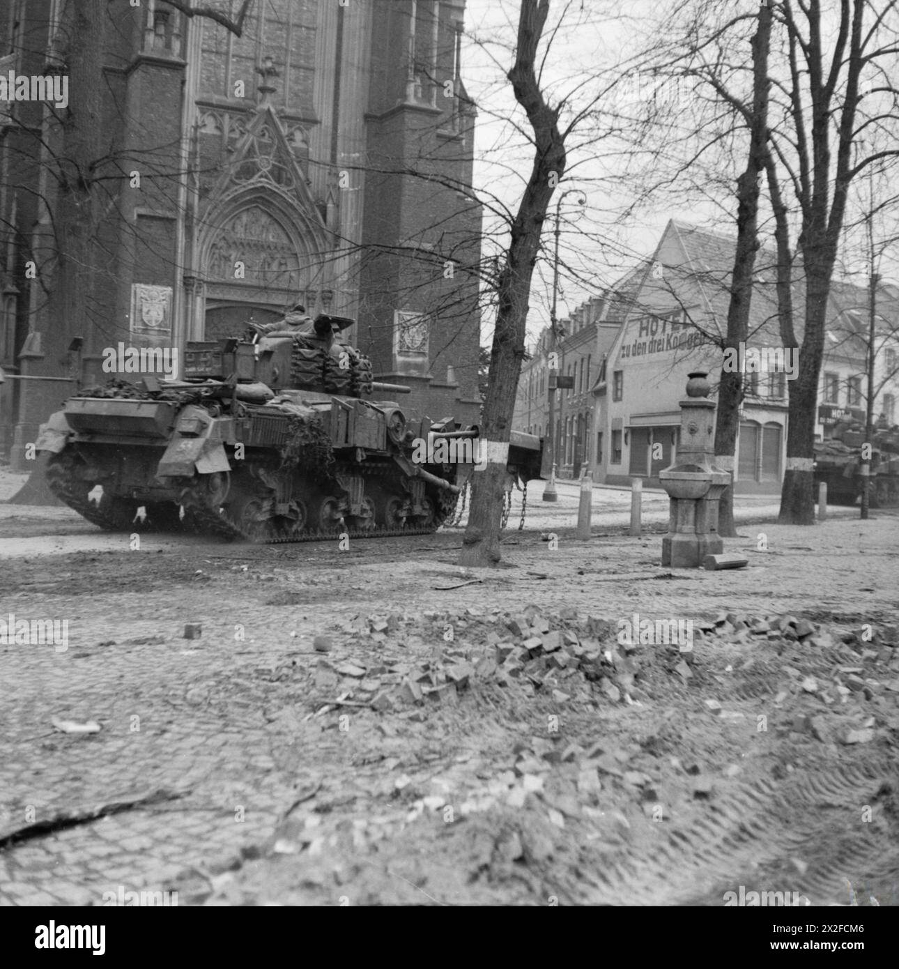 A Sherman Crab flail tank of the 8th Armoured Brigade passes a church ...