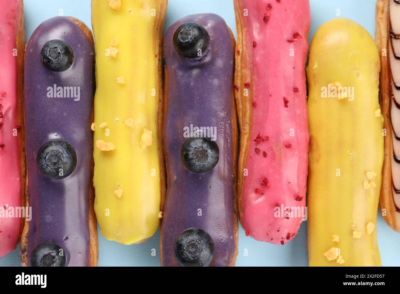 Delicious eclairs covered with glaze on light blue background, top view ...