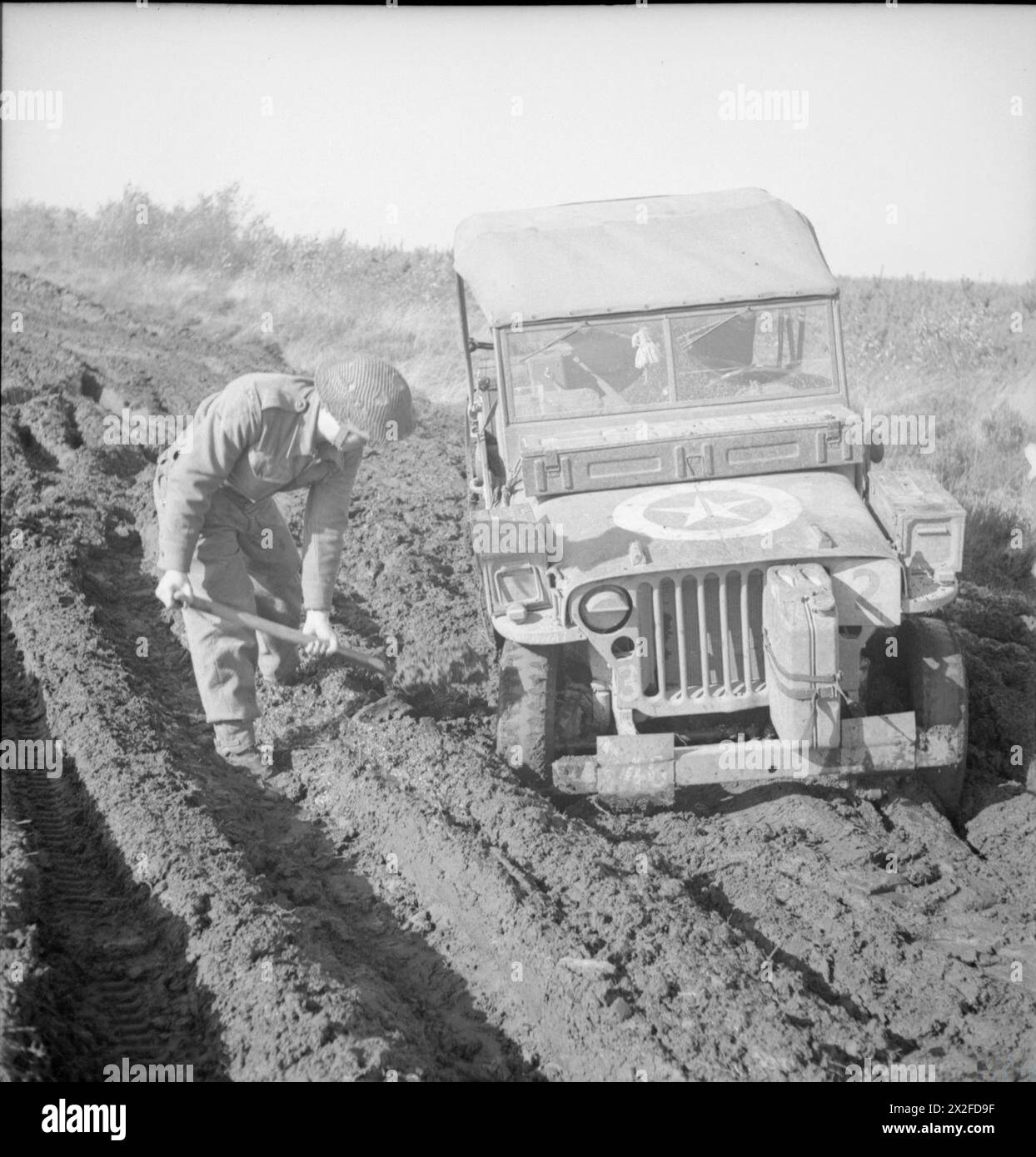 A soldier of the 11th Armoured Division digs out his jeep stuck on a ...