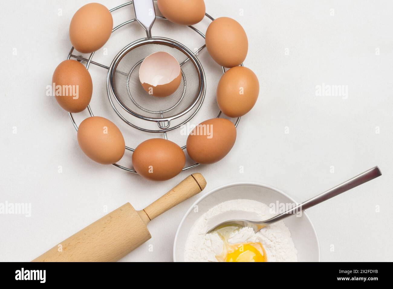 Brown eggs on metal stand. Egg yolk with flour and spoon in bowl. Milk ...