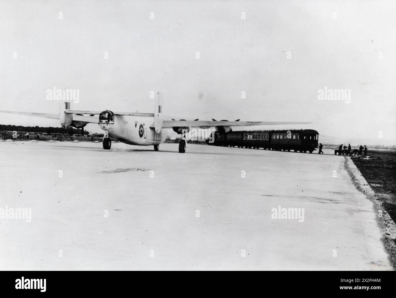 A road train drives past an RAF B-24 Liberator in Britain during 1942 ...