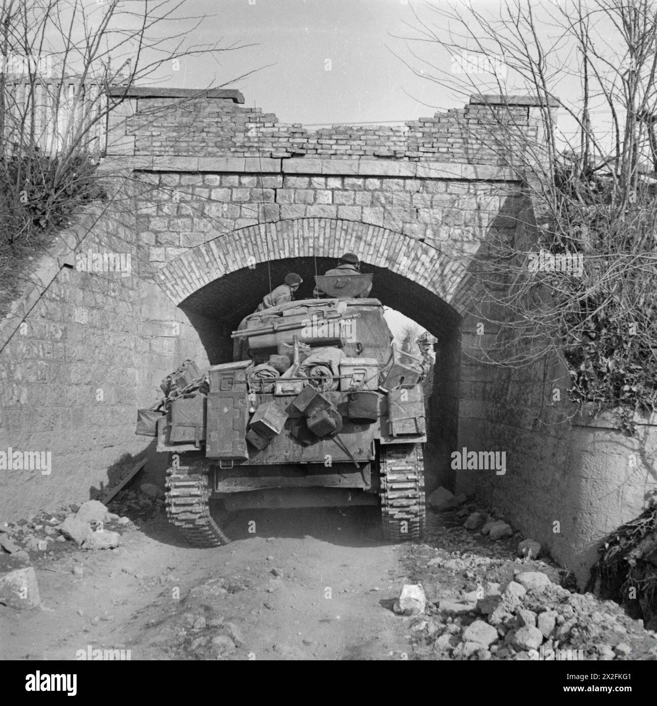 A British Sherman tank passes under a low railway bridge while ...