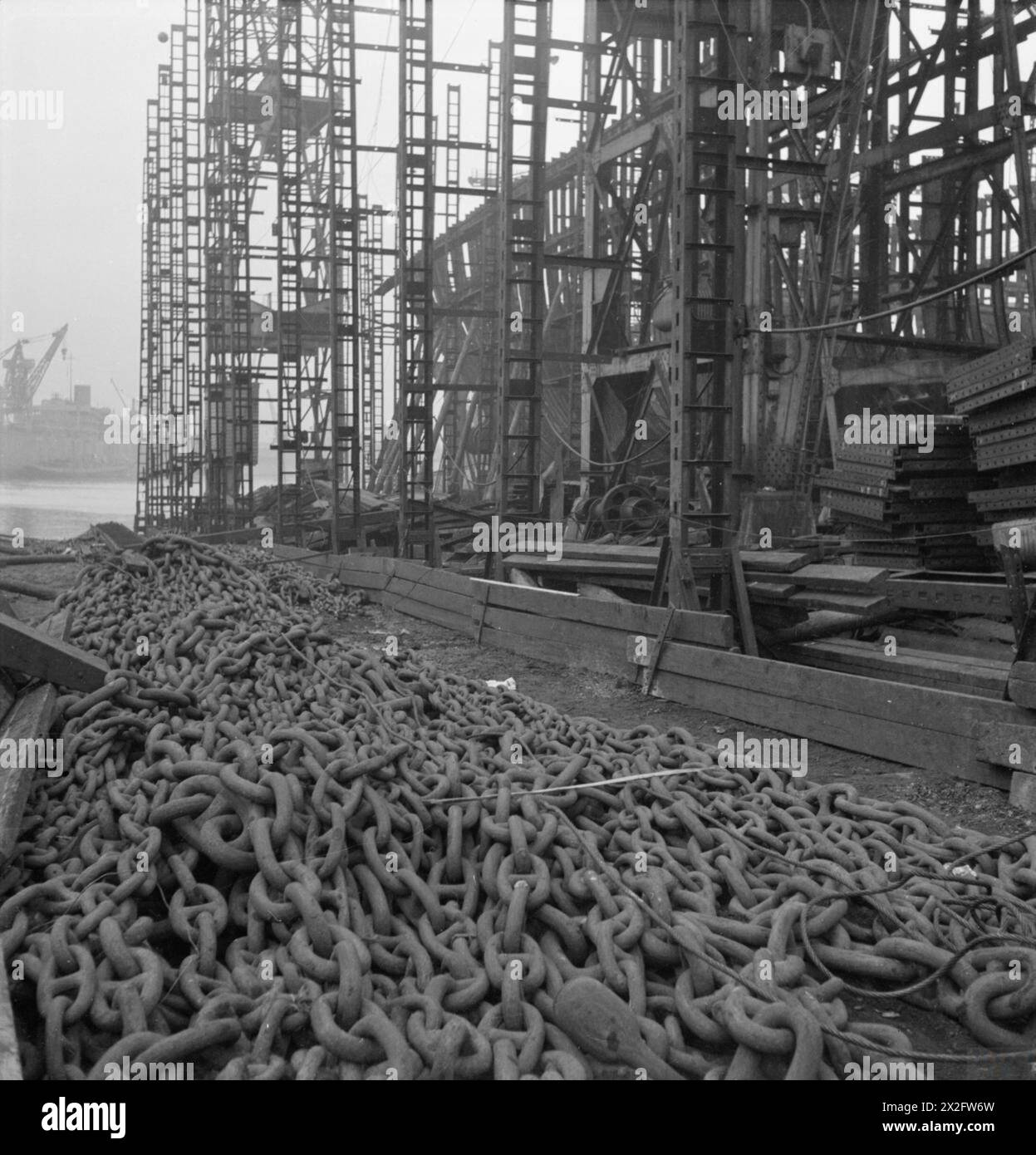 Drag chains are stacked in the foreground of a shipyard at Tyne in 1943 ...