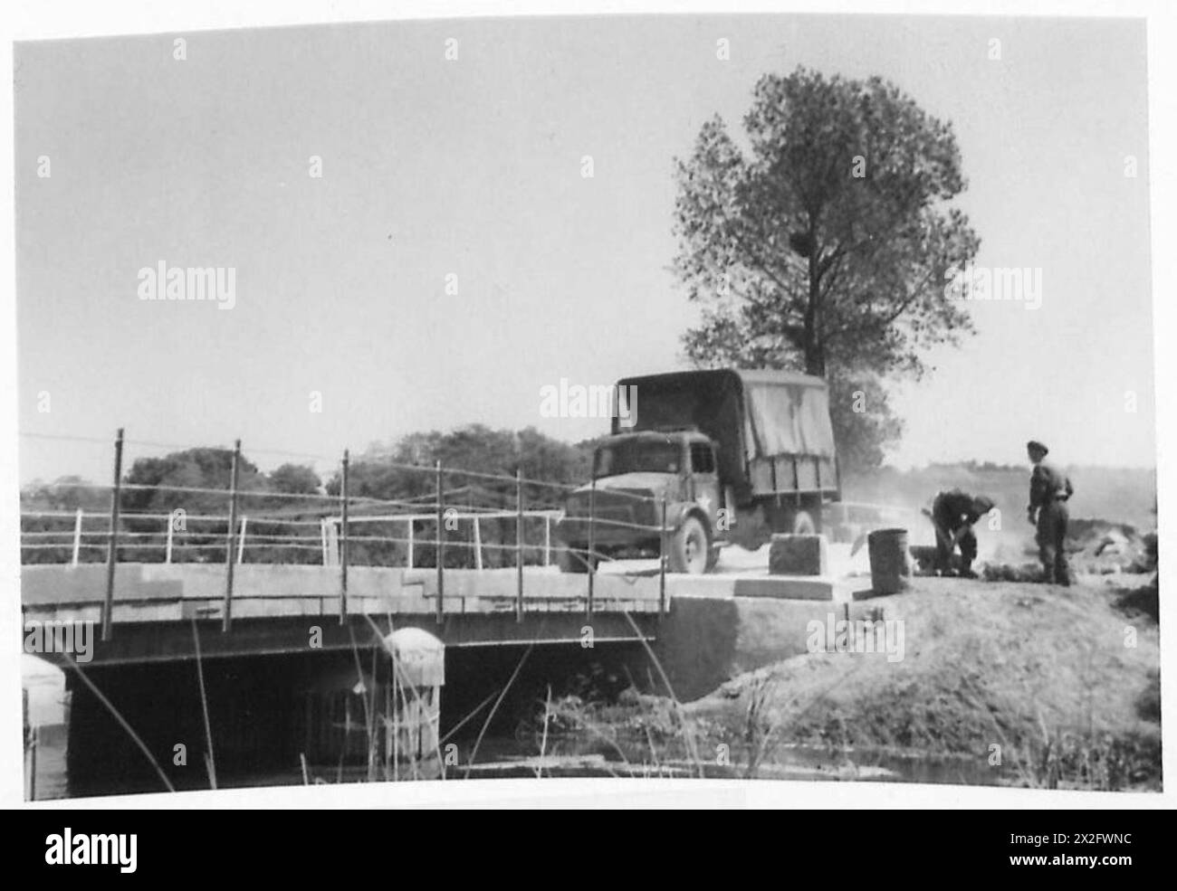 A British Army vehicle crosses a relief bridge over the Seulles River ...