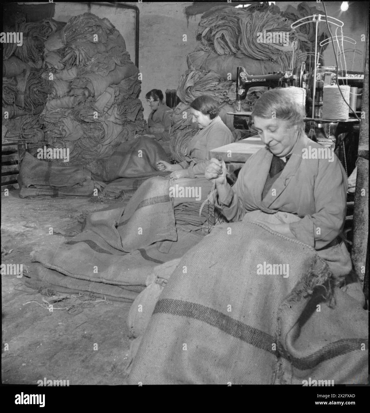 Three women stitch jute sacks by hand at a sack recovery depot in ...