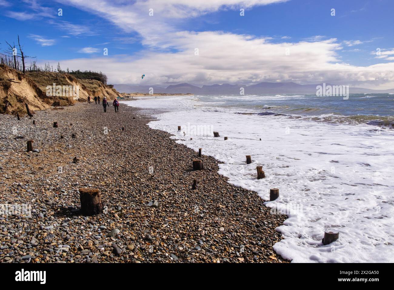 People walking on Newborough beach at high tide looking towards cloud ...