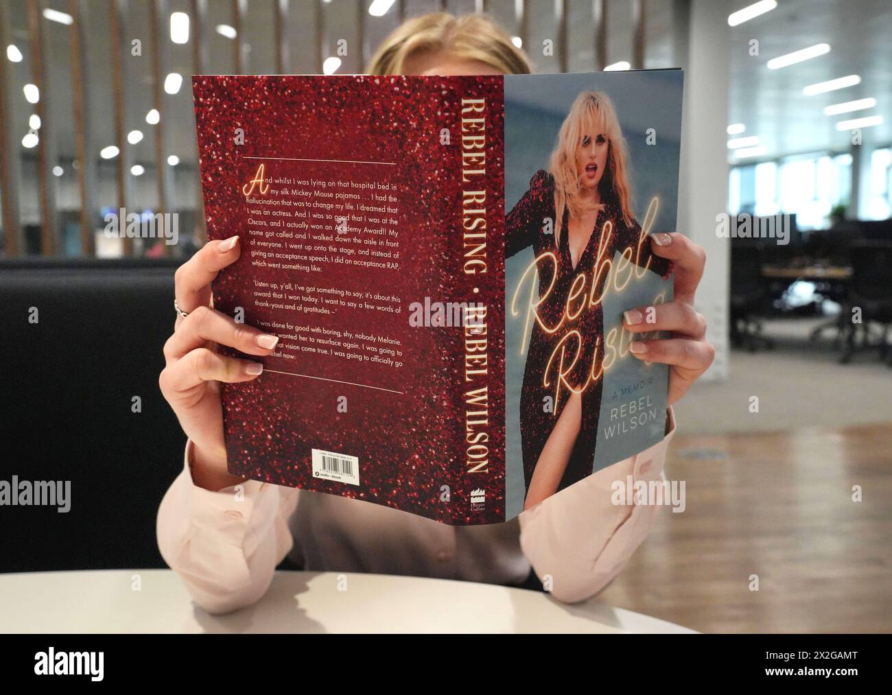 A woman reading a copy of Rebel Rising by Rebel Wilson, the headline ...
