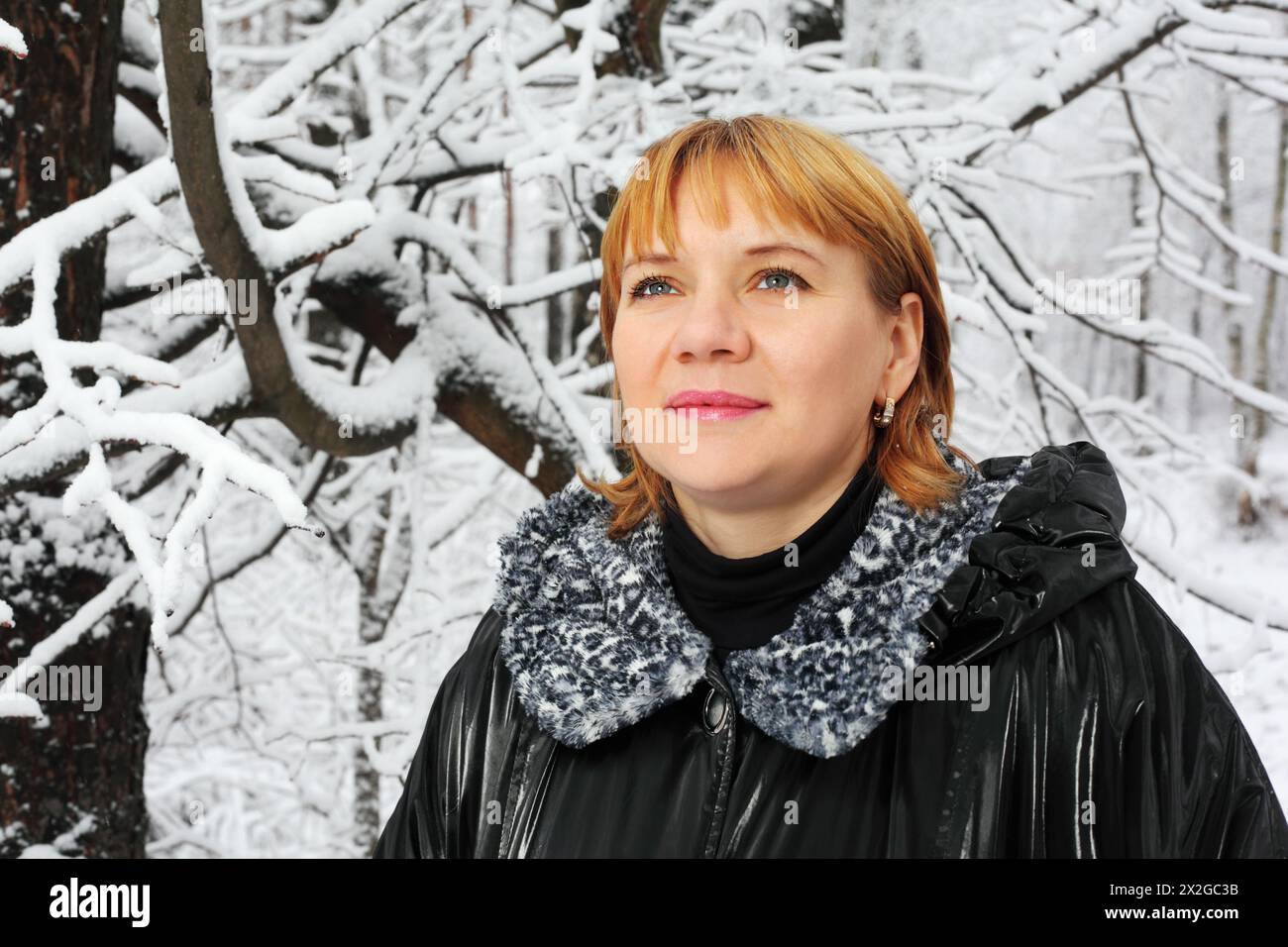 Red-headed woman dressed black jacket look up in woods in snow at ...