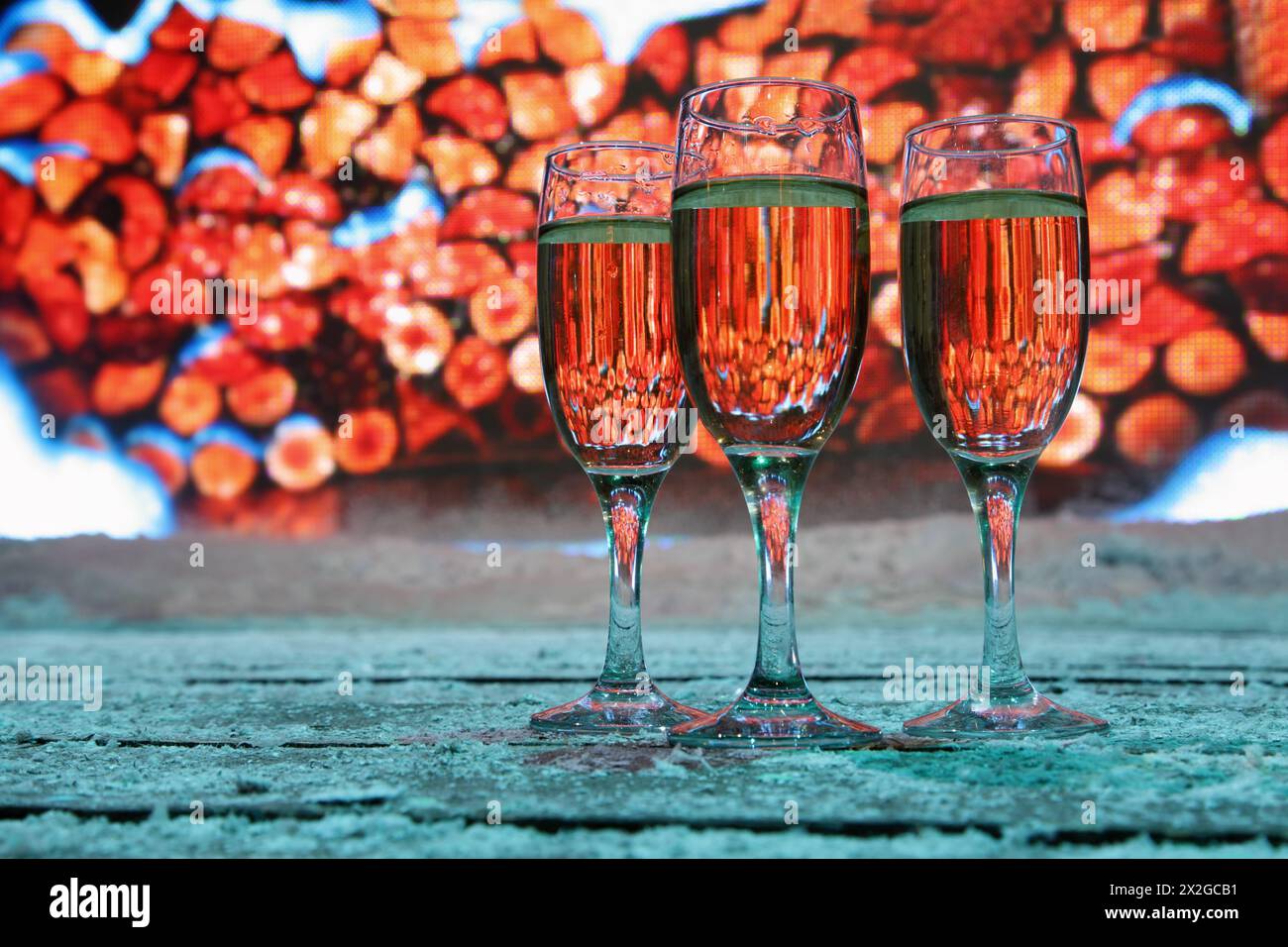 Three glasses of champagne stand near big screen, stack of wood on ...