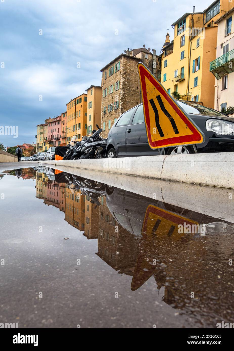 Road narrowing traffic sign, cars and houses in Menton reflect in a ...