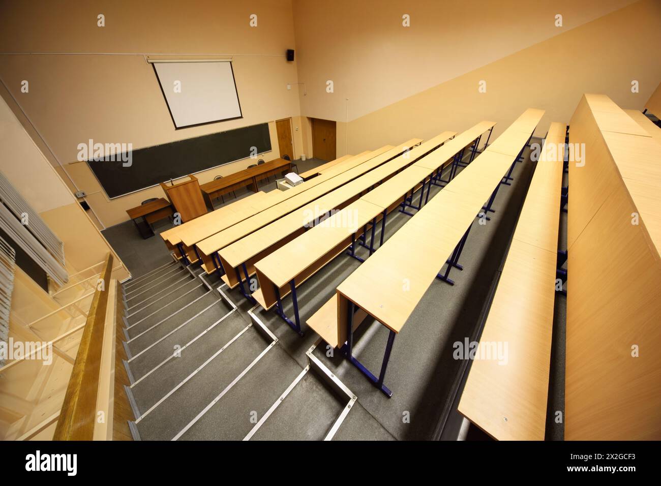 Inside university lecture hall; staircase, wooden desks and benches ...