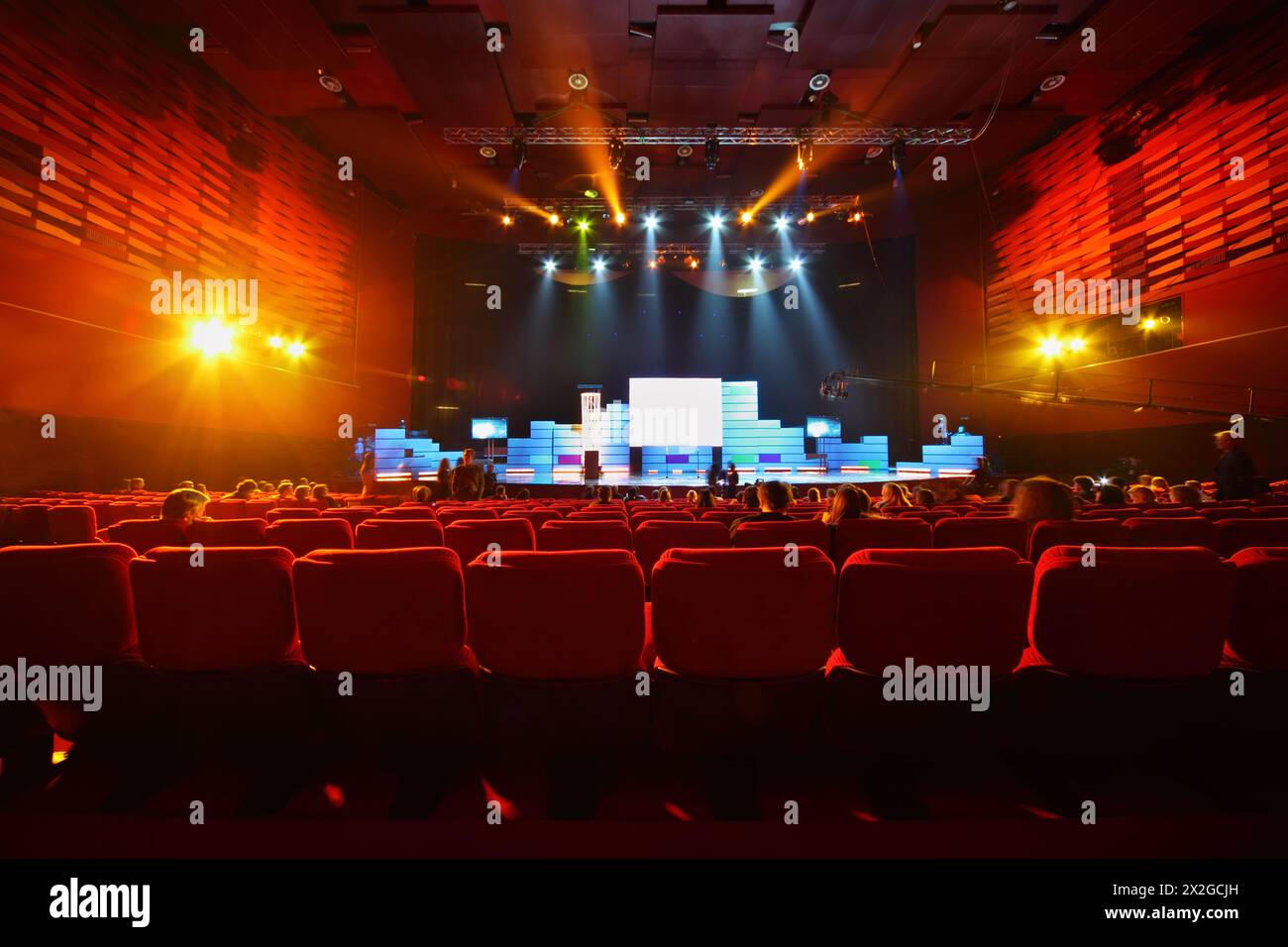 big auditorium with red seats, illuminated scene, people in auditorium ...
