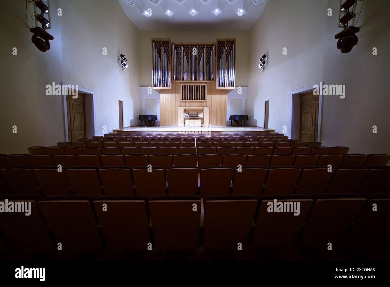 Massive wooden pipe organ in empty large concert hall; rows of seats ...