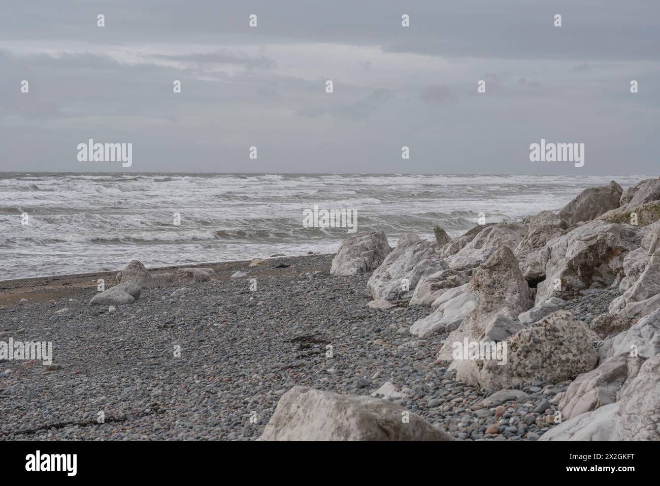 White rocks on a stony beach under grey sky with white water rolling ...