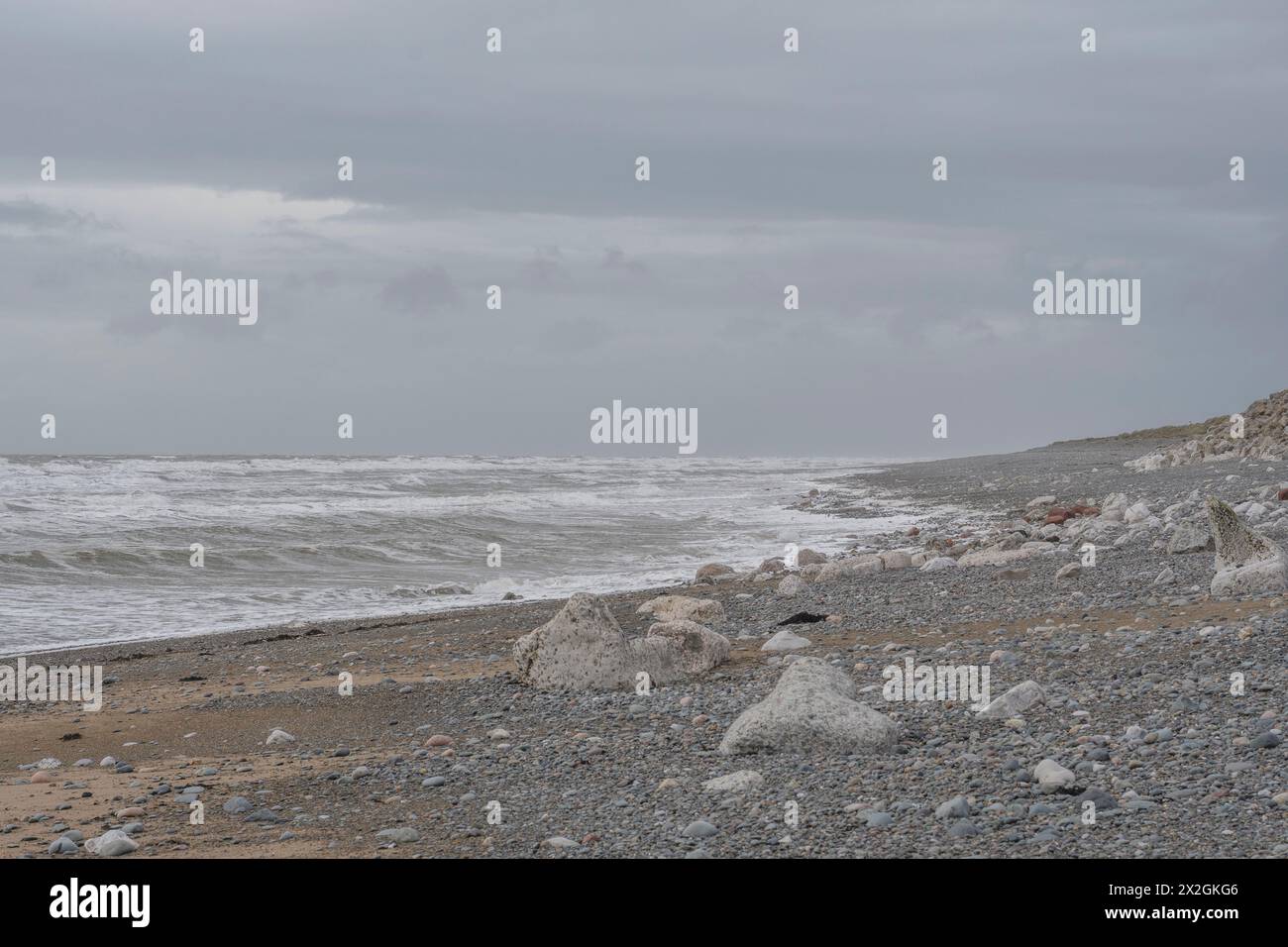 White rocks on a stony beach under grey sky with white water rolling ...